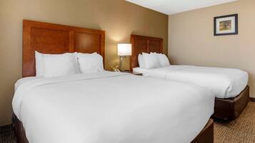 Quarto de hotel com duas camas, mesa de cabeceira com abajur e um quadro na parede.