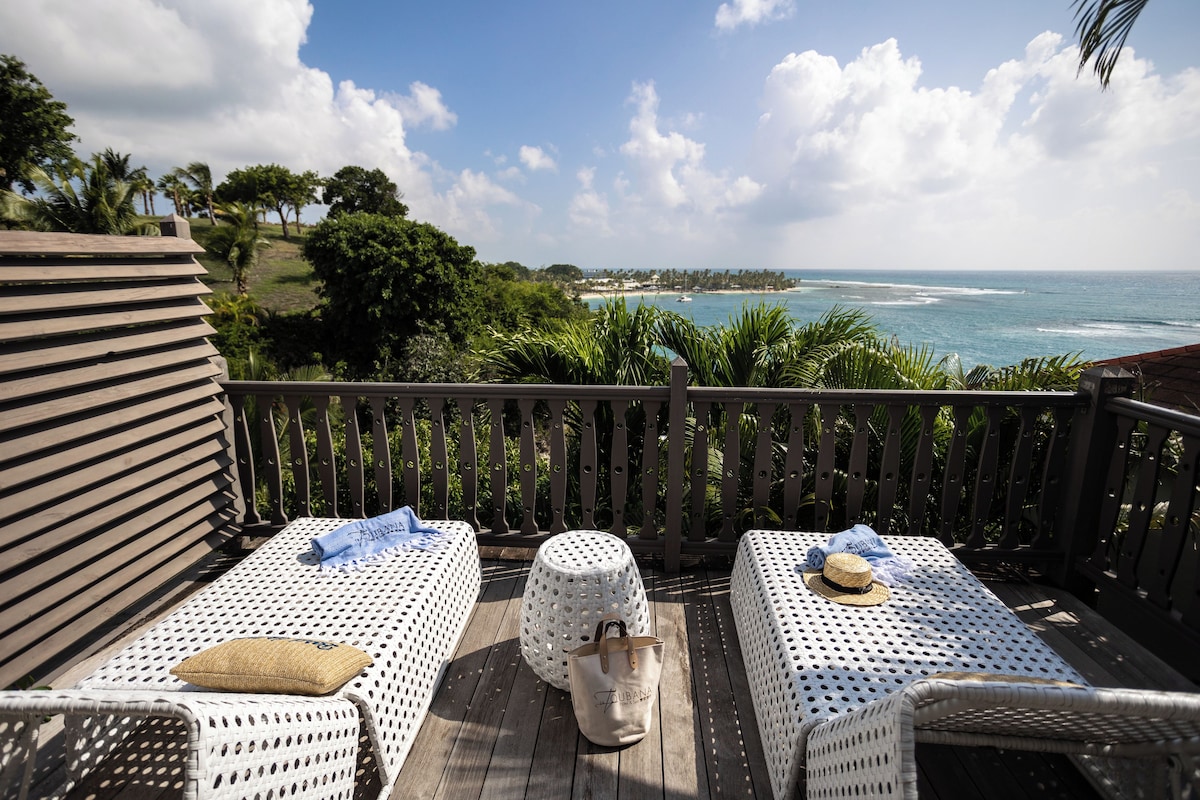 Um terraço com duas poltronas de vime brancas, uma mesa redonda e vista para o oceano.