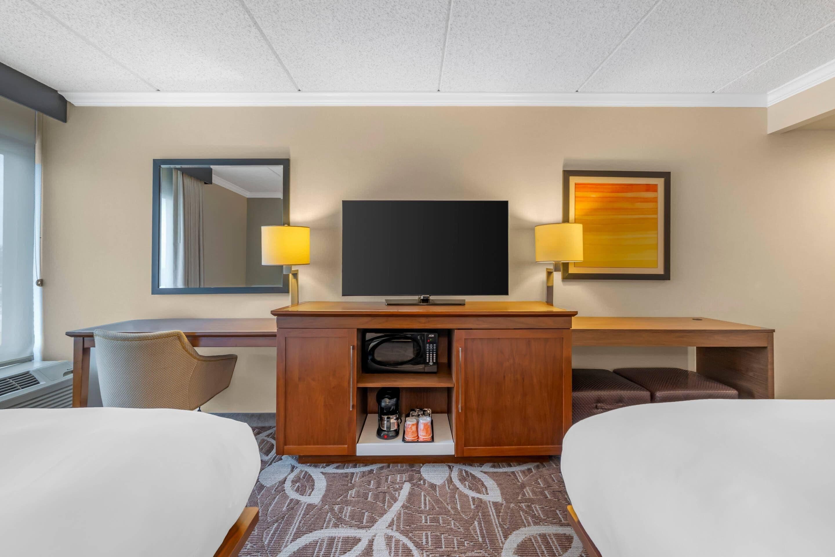 Quarto de hotel com cama, escrivaninha com televisão, micro-ondas e máquina de café.