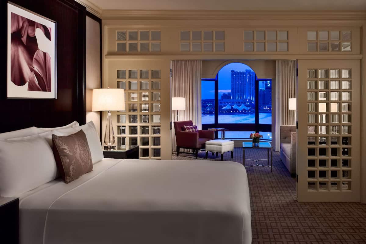 Quarto de hotel com uma cama grande, uma escrivaninha, uma cadeira e vista para a cidade à noite.
