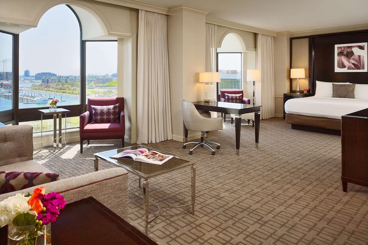 Quarto de hotel com uma janela grande, cama, escrivaninha, cadeira e mesa de centro.