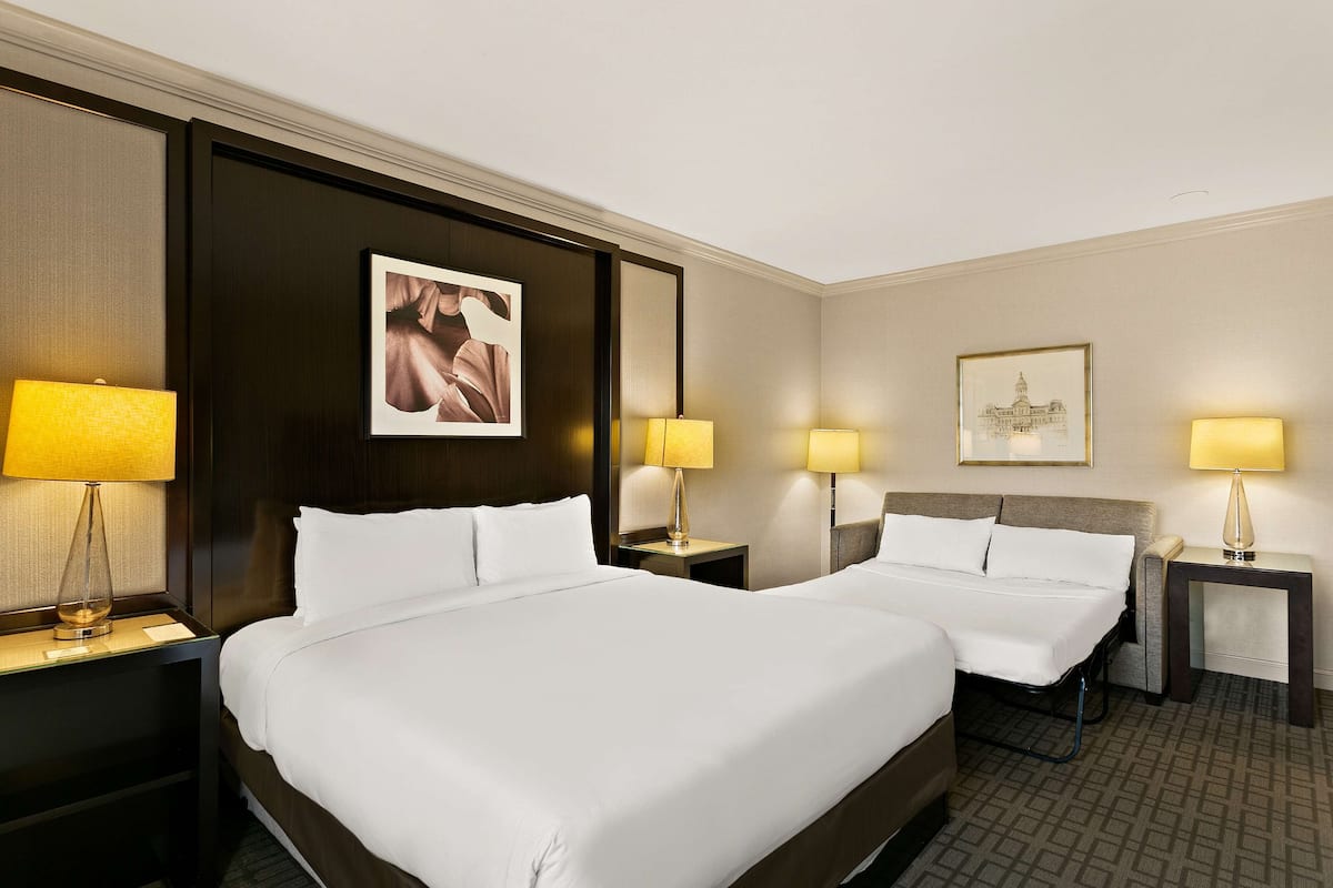 Quarto de hotel com duas camas, um espelho grande e duas mesas de cabeceira com luminárias.