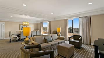 Quarto de hotel com um sofá grande, uma cadeira, uma mesa de jantar com cadeiras e uma televisão.