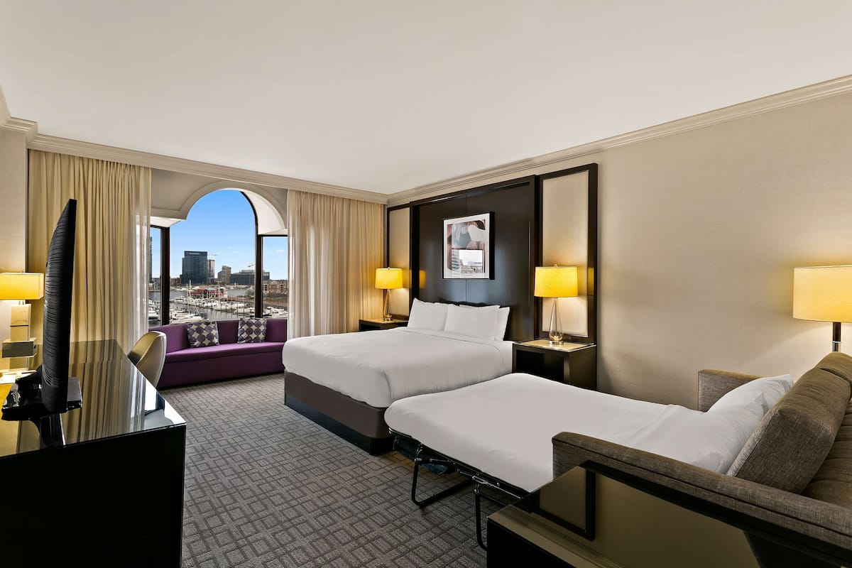 Quarto de hotel com duas camas, um sofá, uma mesa de escritório e uma televisão.