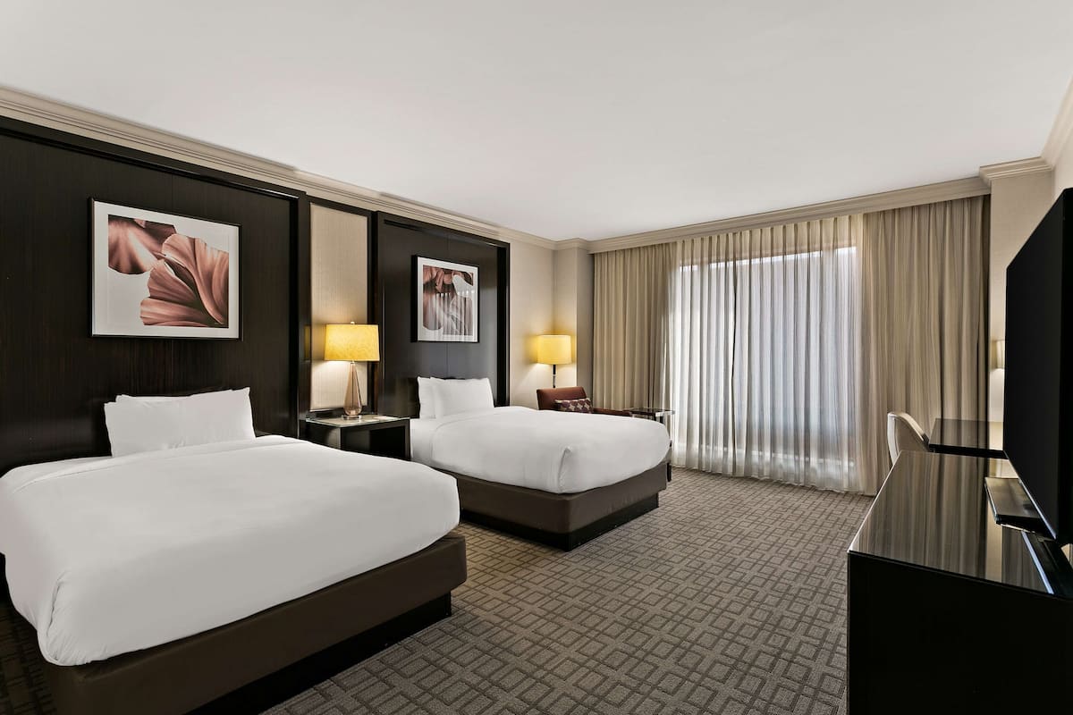 Quarto de hotel com duas camas, uma escrivaninha e uma televisão.