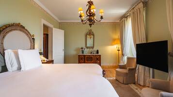 Quarto de hotel com uma cama grande, um candelabro, uma televisão, uma escrivaninha e uma cadeira.