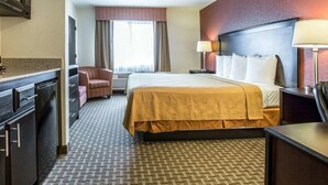 Quarto de hotel com cama, escrivaninha, cadeira, janela com cortinas e micro-ondas.