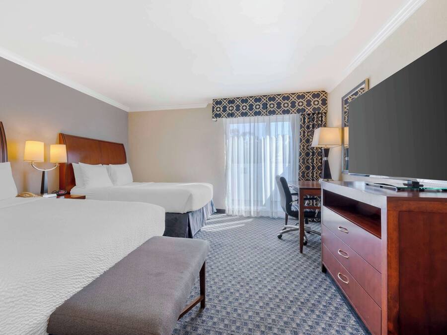 Quarto de hotel com duas camas, uma escrivaninha, uma cadeira, uma televisão e uma luminária de mesa.