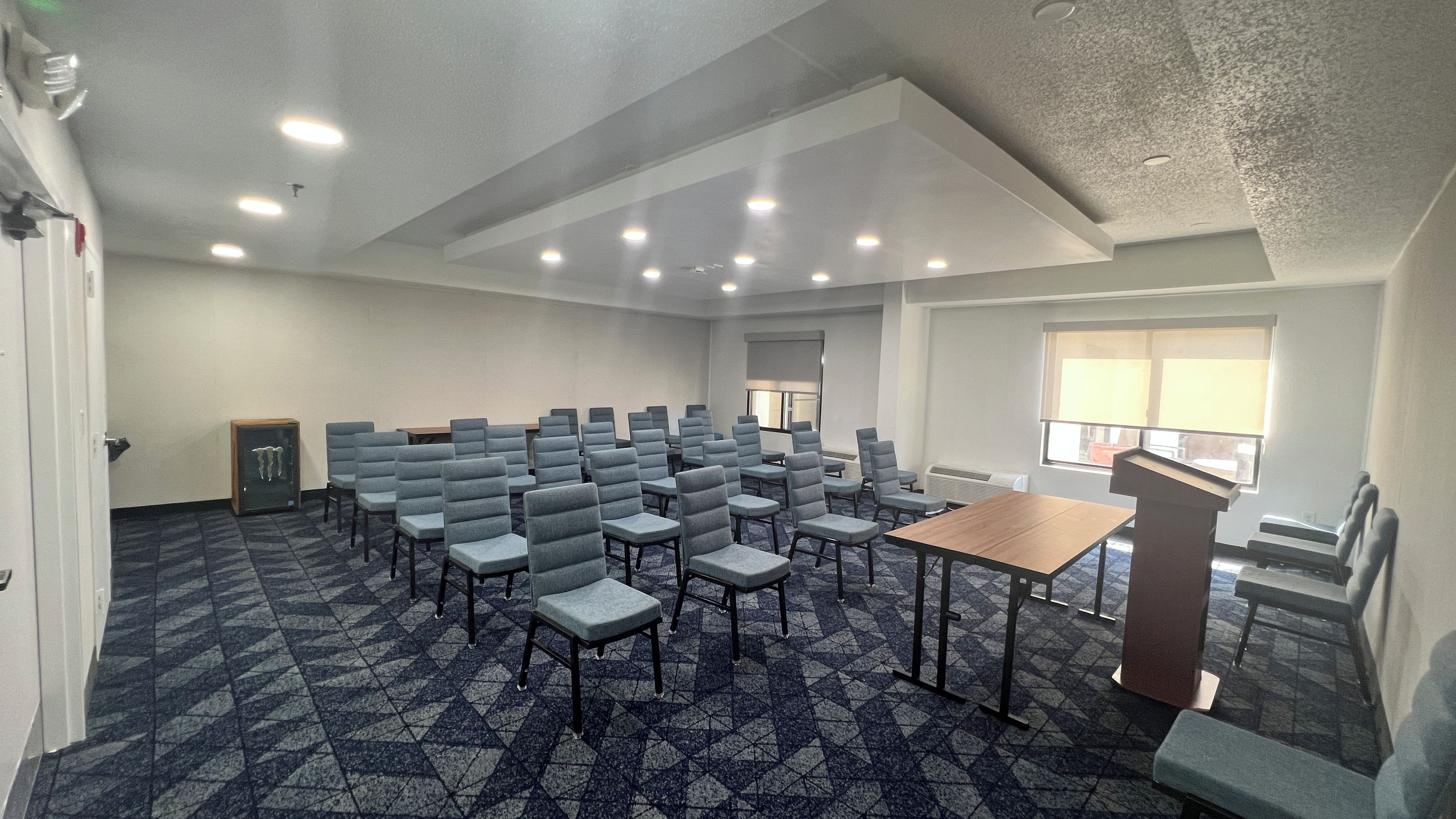 Sala de conferências com fileiras de cadeiras, um palanque e uma grande janela.