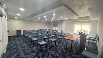 Sala de conferências com fileiras de cadeiras, um palanque e uma grande janela.