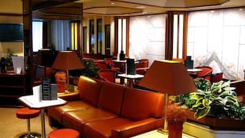 Um saguão de hotel com um sofá de couro, mesas redondas e luminárias.