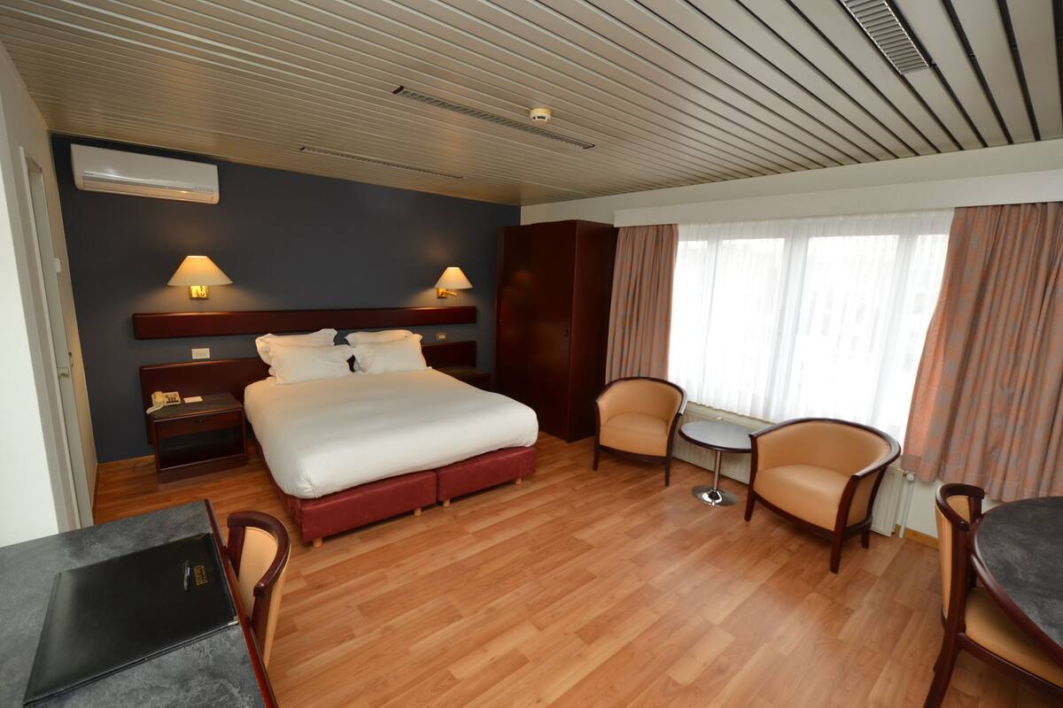 Quarto de hotel com cama, mesas de cabeceira, escrivaninha e uma cadeira.