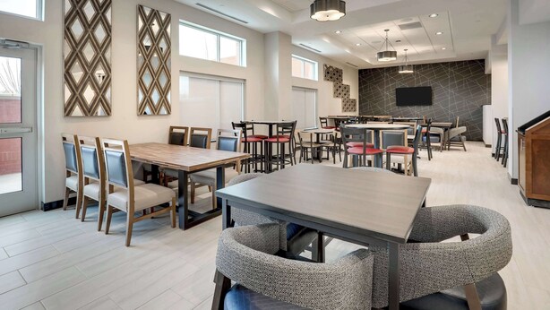 Uma sala de jantar moderna com várias mesas e cadeiras, área de cozinha com televisão de tela plana e painéis decorativos na parede.