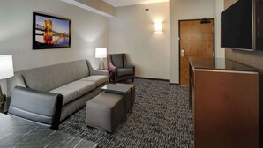 Quarto de hotel com sofá, poltrona, banquinho, televisão de tela plana e uma pintura de uma ponte.