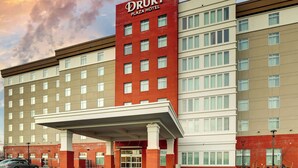 Um hotel Drury Plaza com fachada em vermelho e bege marcante, vários andares e área de entrada coberta.