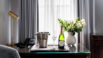 Quarto de hotel com escrivaninha, telefone, garrafa de champanhe, um vaso com flores e uma luminária.