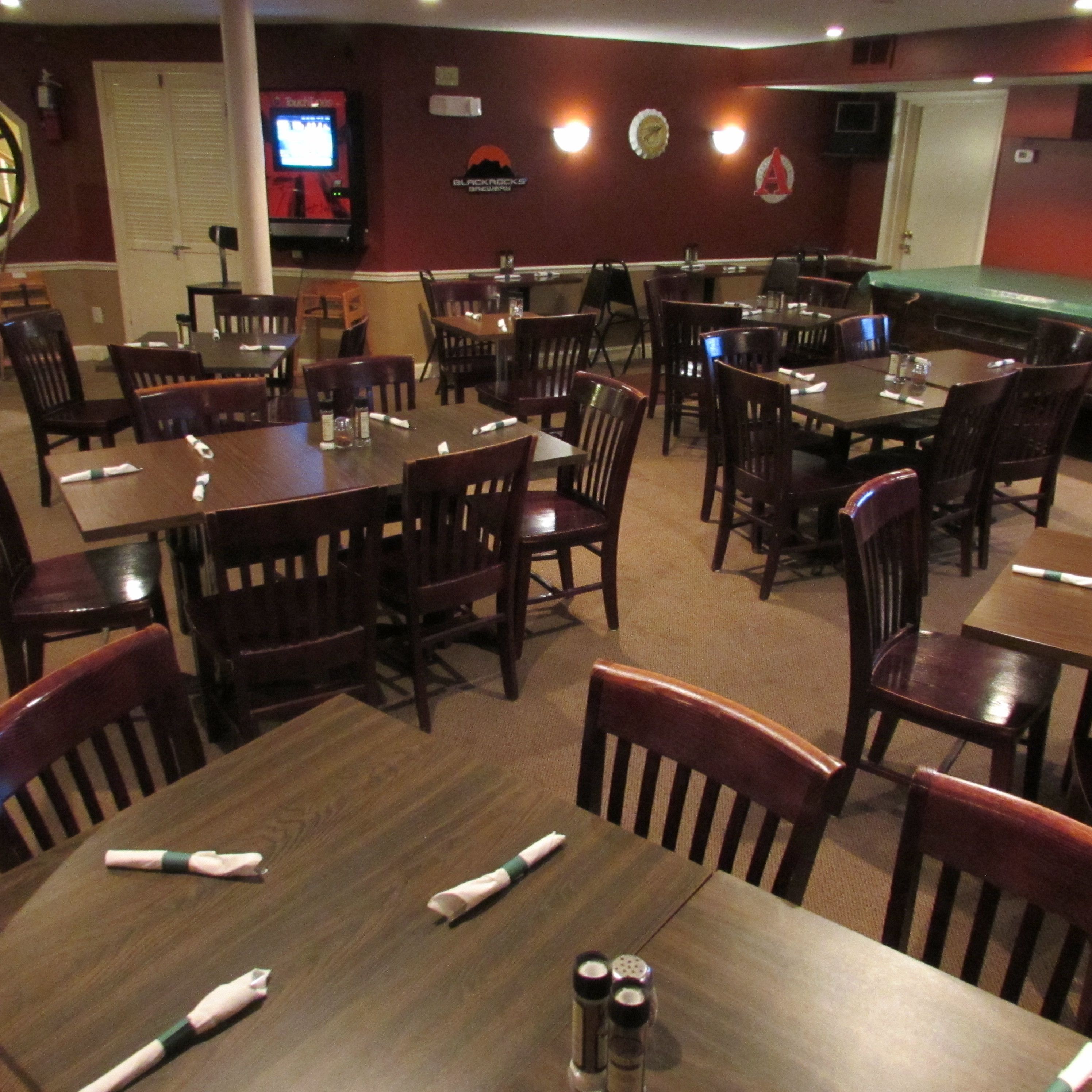 Um restaurante com várias mesas e cadeiras, uma tela de televisão e um relógio na parede.