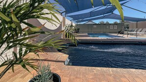 Uma área de piscina com um deck de tijolos, piscina azul e área coberta por um toldo azul.