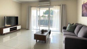 Sala moderna com televisão de tela plana, sofá, mesa de centro e varanda com vista para o verde.