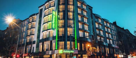 Um hotel com vários andares e fachada curva, com sinalização iluminada e vista da rua com rastros de luz.