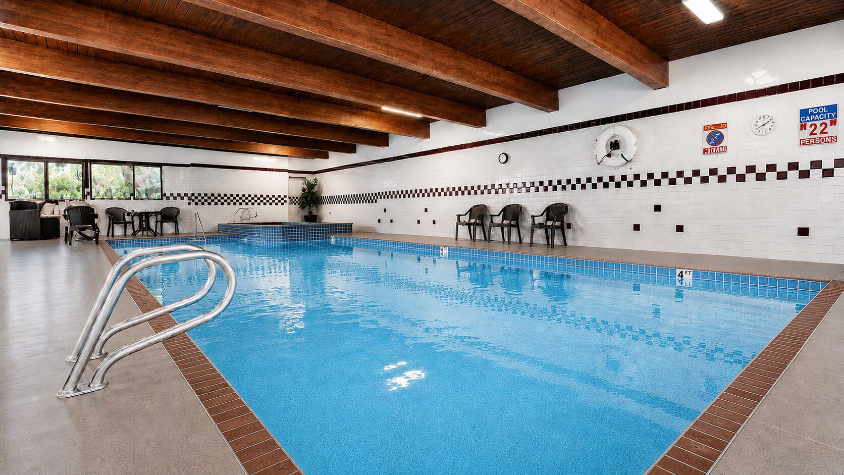 Piscina interior com capacidade para 22 pessoas, cadeira de salva-vidas e relógio na parede.