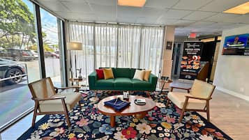 Um saguão de hotel com um sofá verde, duas poltronas, uma mesa de centro e um tapete floral.