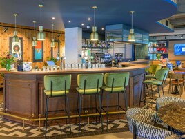 Uma área de bar com balcão, banquetas e um espaço de estar com cadeiras estampadas.