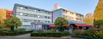 Um hotel moderno com fachada plana, várias janelas e toldo vermelho sobre a entrada.