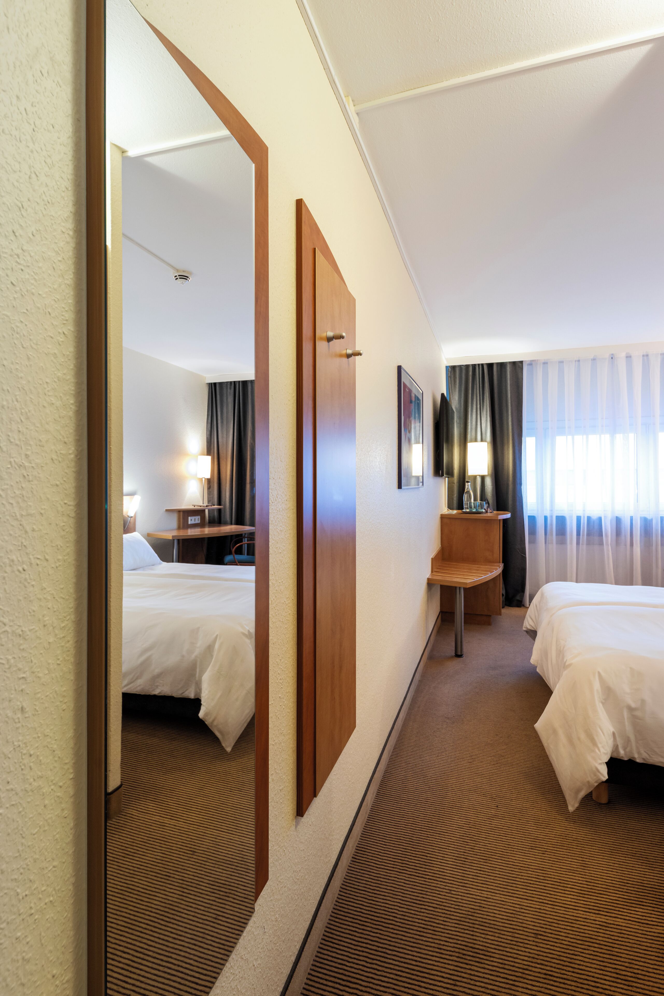 Quarto de hotel com duas camas, um espaço de estar com uma poltrona, uma mesa de escritório e um espelho grande.