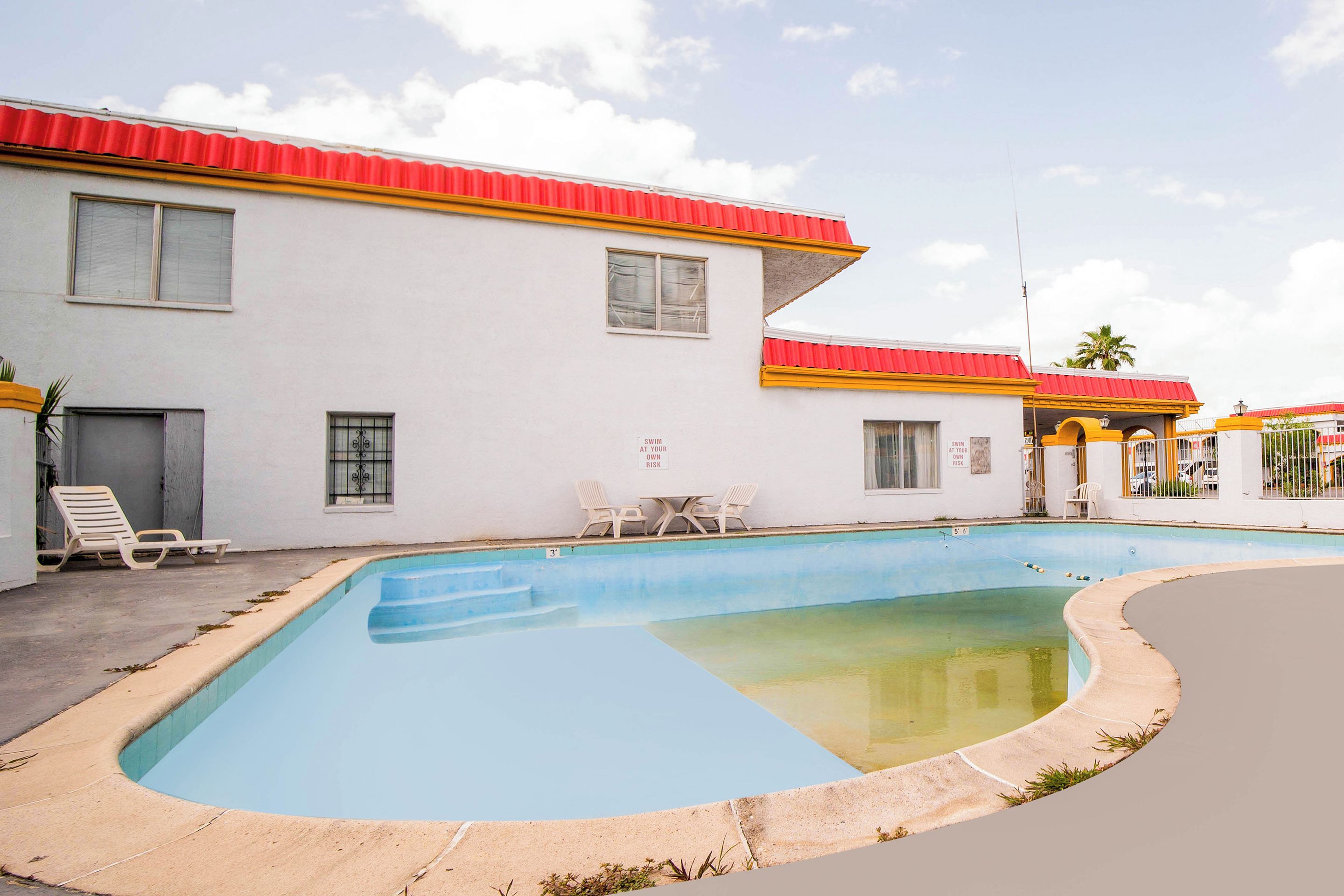 Piscina com um edifício de telhado vermelho ao fundo.