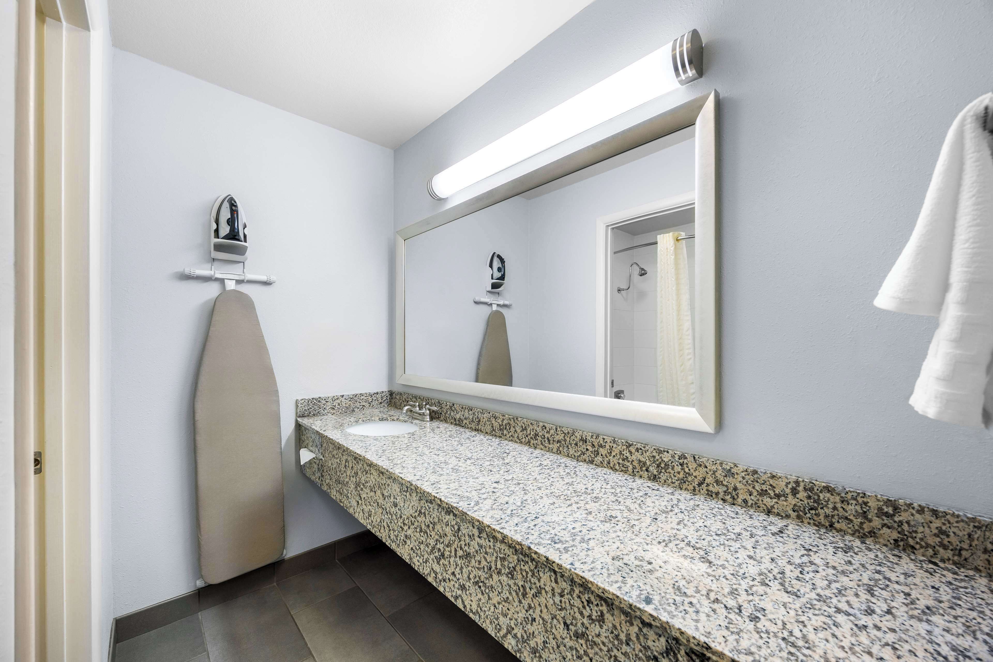 Casa de banho com bancada de granito, lavatório branco, espelho e toalha pendurada na parede.