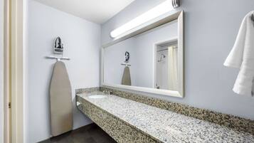Casa de banho com bancada de granito, lavatório branco, espelho e toalha pendurada na parede.