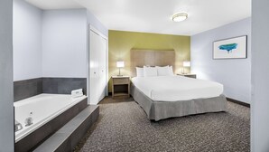 Quarto de hotel com cama grande, banheiro separado, mesa de cabeceira com luminária e quadro na parede.