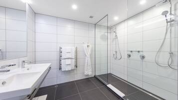 Uma casa de banho moderna com duas pias, cabine de duche em vidro e um roupão branco pendurado na parede.