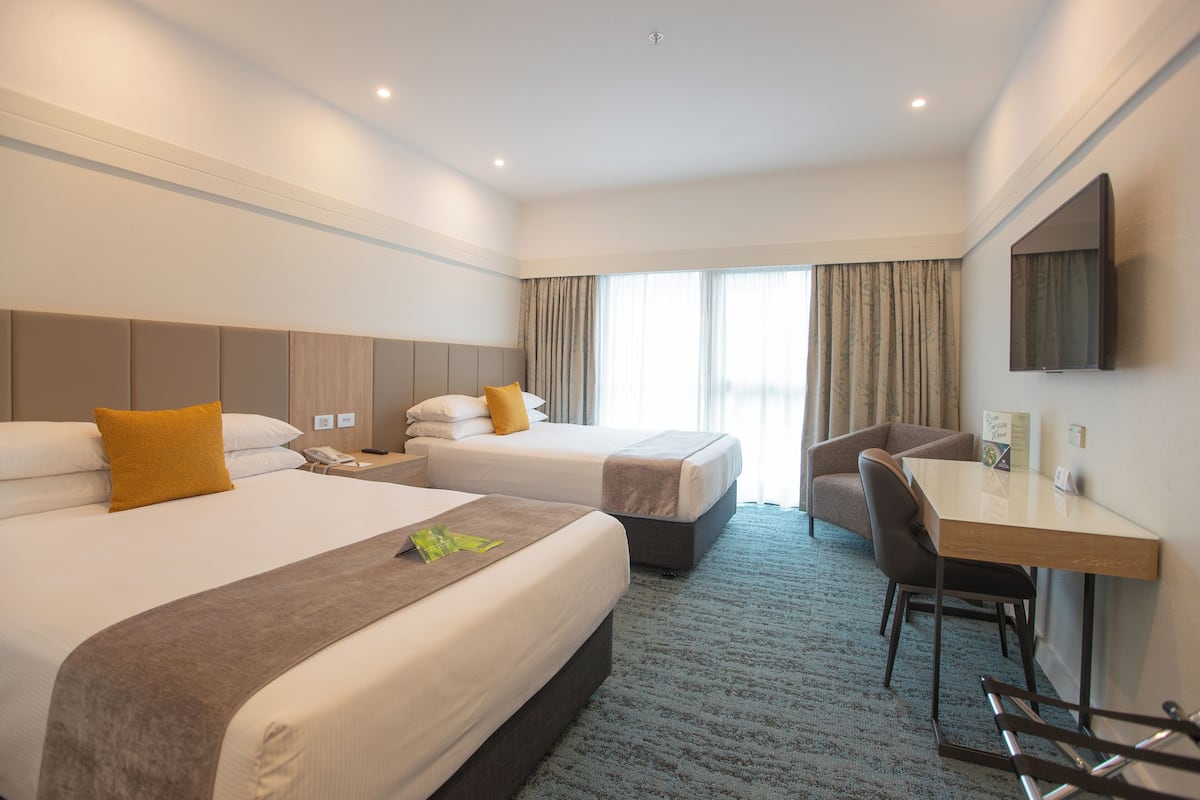 Quarto de hotel com duas camas, uma escrivaninha, uma cadeira e uma televisão.