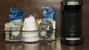 Uma cafeteira e uma cesta com diversos objetos sobre uma superfície de madeira.