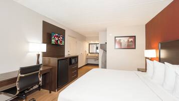 Quarto de hotel com cama, escrivaninha, cadeira, televisão e um banheiro visível ao fundo.