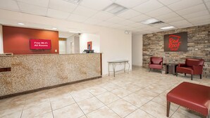 Uma área de recepção com um letreiro indicando 'Wi-Fi Gratuito em Todos os Quartos', uma parede de pedra com a sinalização 'Red Roof Inn' e um espaço de estar com duas cadeiras e um banco.