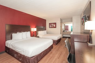 Quarto de hotel com duas camas, uma escrivaninha, uma cadeira, um abajur e um quadro na parede.