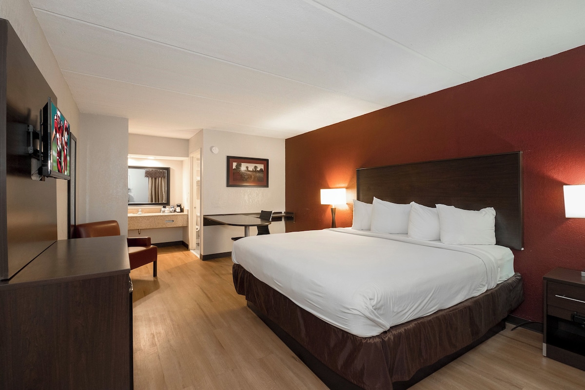 Quarto de hotel com uma cama grande, uma escrivaninha, uma cadeira, um espelho e uma televisão.