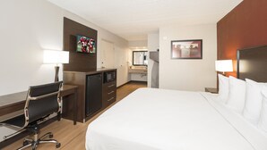 Quarto de hotel com cama, escrivaninha, cadeira, televisão, micro-ondas e uma pequena copa.