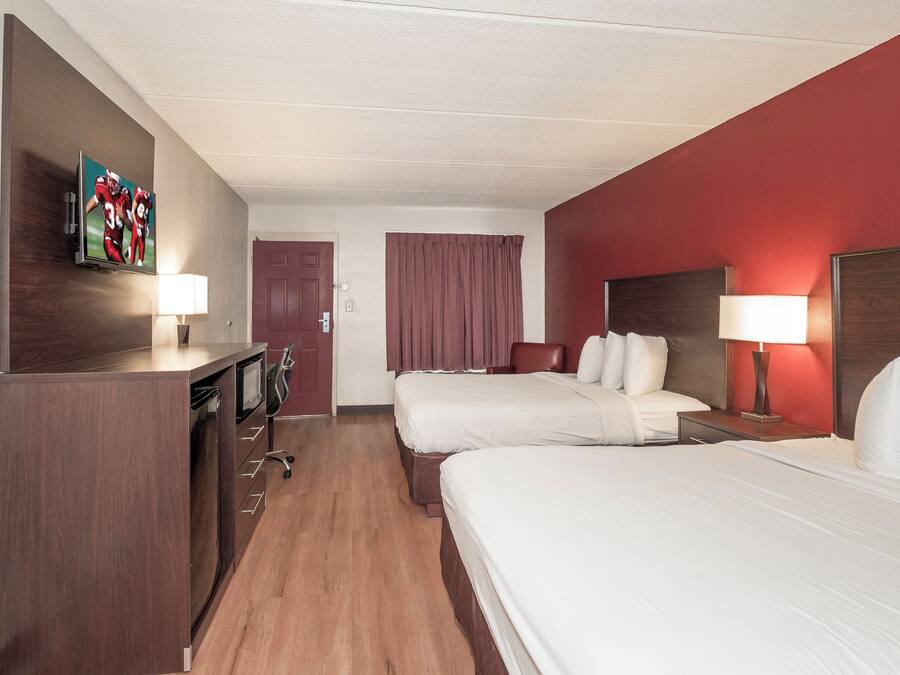 Quarto de hotel com duas camas, uma escrivaninha, televisão de tela plana, uma cadeira e uma janela com cortinas.