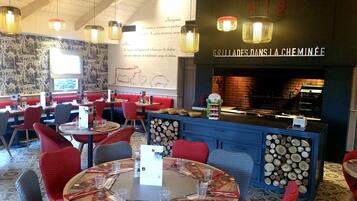 Interior de restaurante com assentos vermelhos, balcão preto com grelha e quadro de menu.