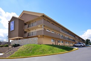 Um hotel com vários andares, fachada de pedra, varandas e estacionamento.