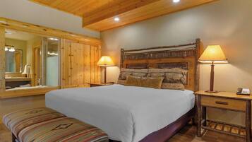 Quarto com uma cama grande, cabeceira de madeira, duas mesas de cabeceira com luminárias, um banco e um espelho.