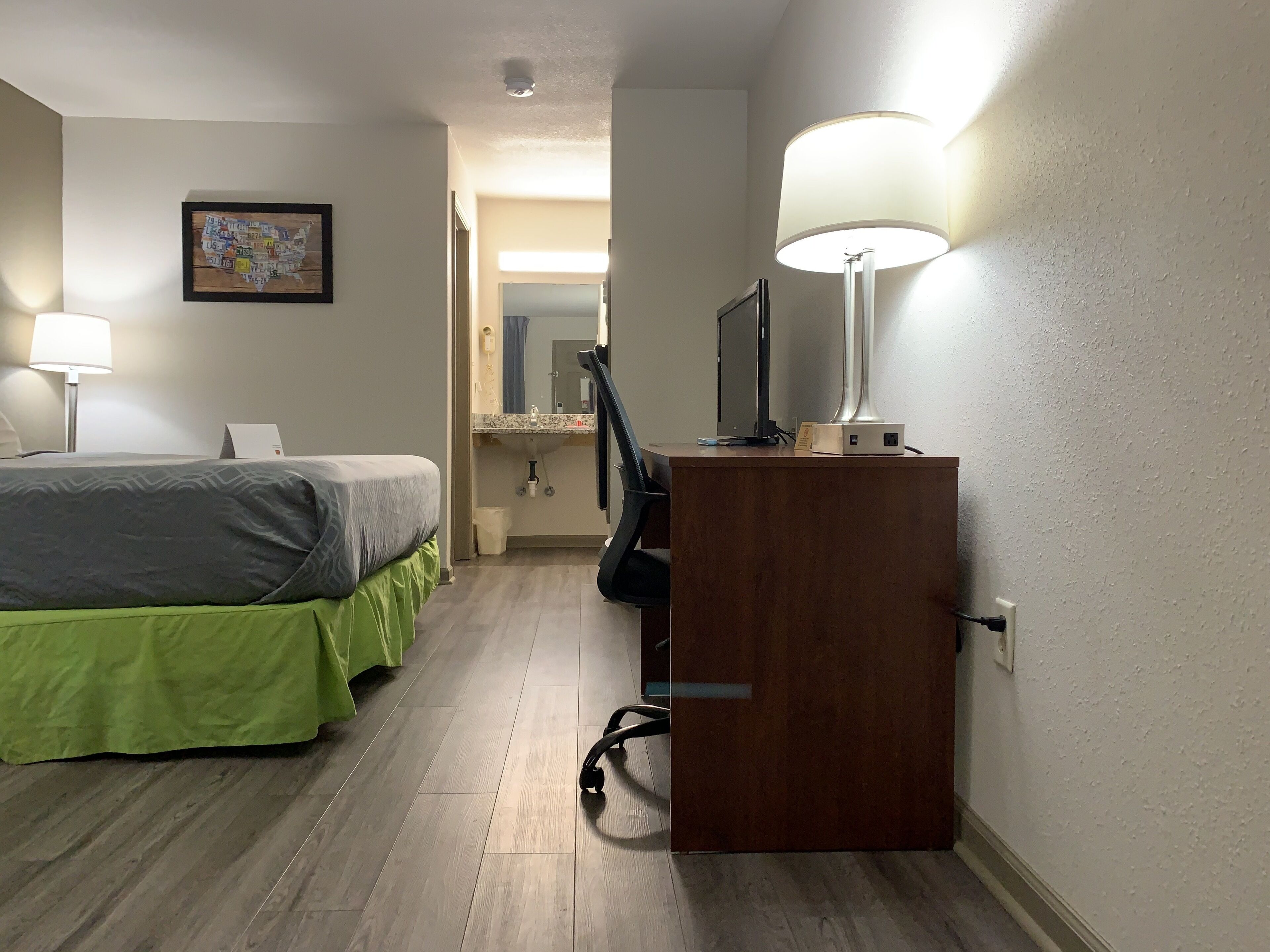 Quarto de hotel com cama, escrivaninha, cadeira e abajur.