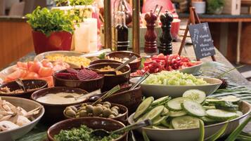 Mesa de buffet com diversos alimentos, incluindo frutas, legumes e patês.