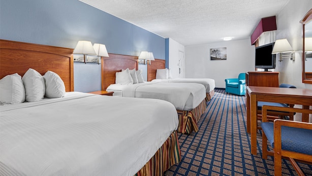 Quarto de hotel com três camas, uma escrivaninha, uma cadeira e uma televisão.