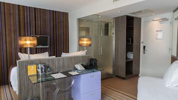Quarto de hotel com uma cama, uma escrivaninha com computador, uma televisão e um guarda-roupa.