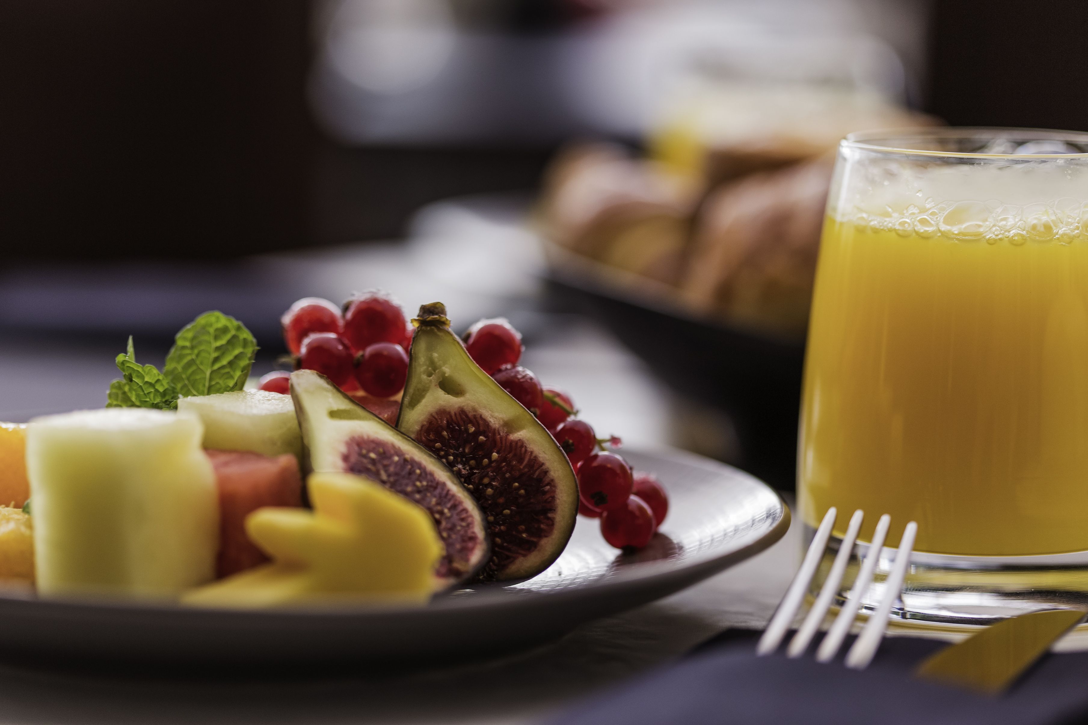 Um prato com frutas variadas e um copo de suco de laranja sobre uma mesa.
